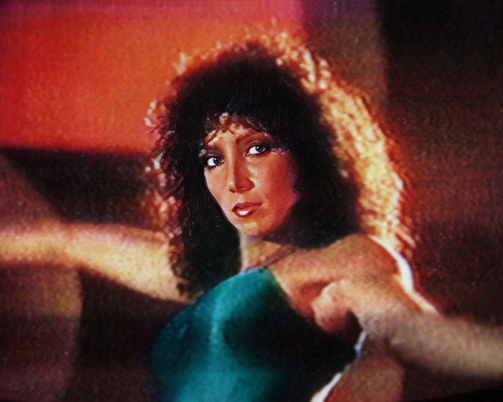 Curly-haired woman in blue top with makeup against vibrant backdrop ...